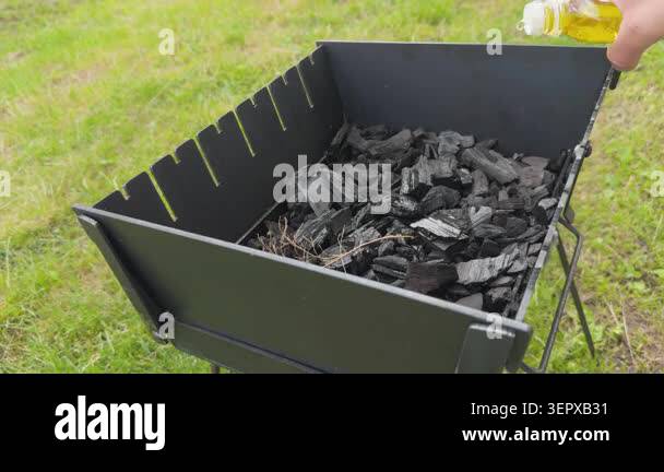 Man's hand pouring flammable liquid onto charcoal in a metal brazier ...