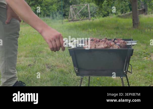 Male hand turning skewers with marinated pork meat grilling on a ...