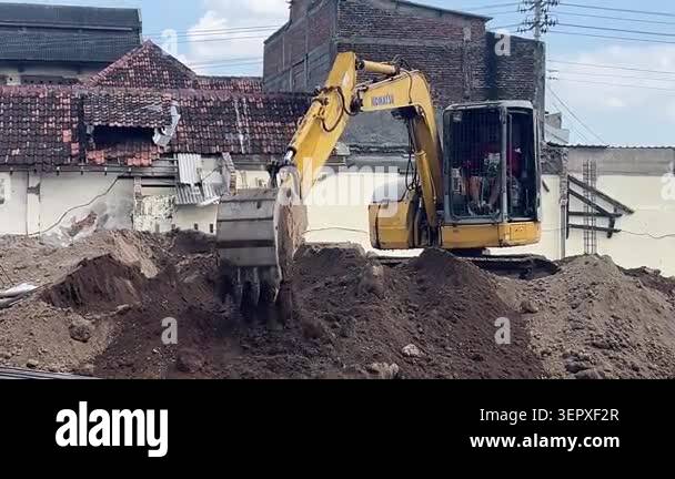 A bright yellow excavator operates on a dirt pile against a background ...