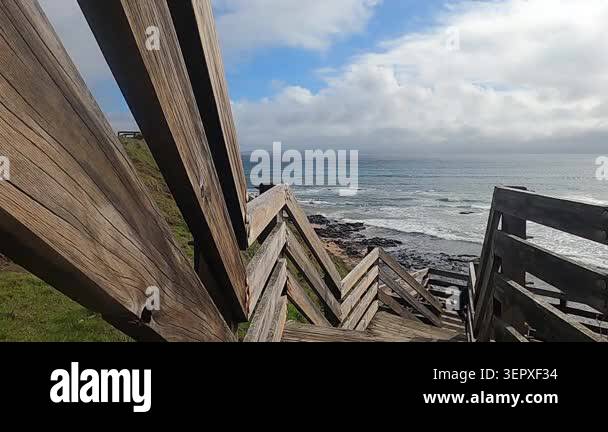 A wooden staircase descends toward a rocky shoreline, offering a wide ...