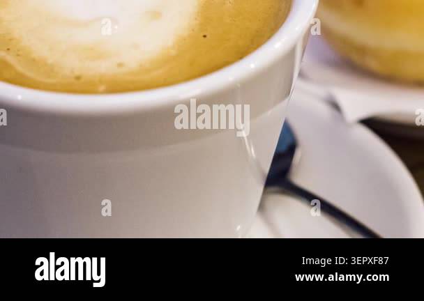 Close-up of a white cup of coffee with creamy foam on a saucer and ...