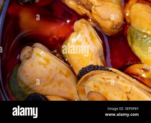 Close-up top view of mussels in red marinade or oil inside a glass jar ...
