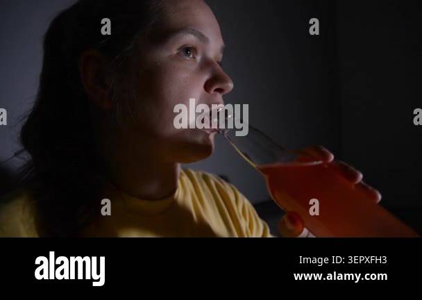 Close up of a young woman drinking kombucha in a dark room illuminated ...