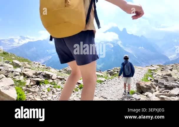Two people with backpacks hiking on a rocky mountain trail with a ...