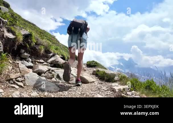 A person with a backpack is hiking up a rocky mountain trail with a ...