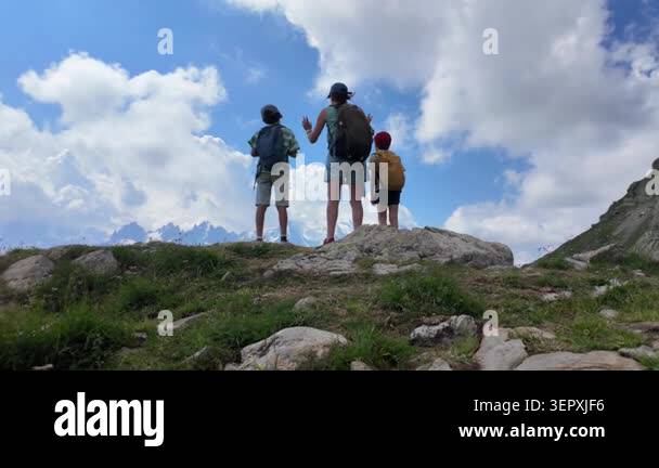 A woman and two children stand on a rocky mountain peak, looking out at ...