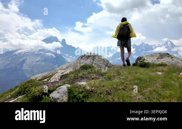 A person wearing a yellow jacket and backpack walks on a grassy ...