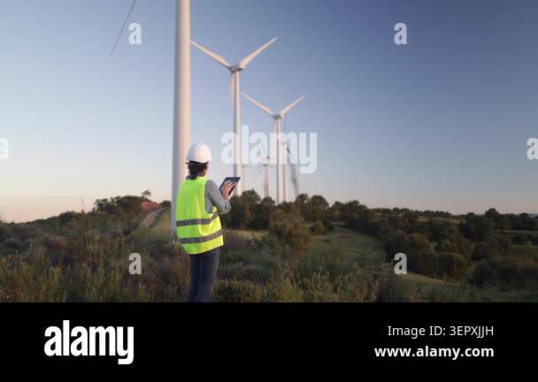 A woman in a hard hat and safety vest uses a tablet to monitor wind ...