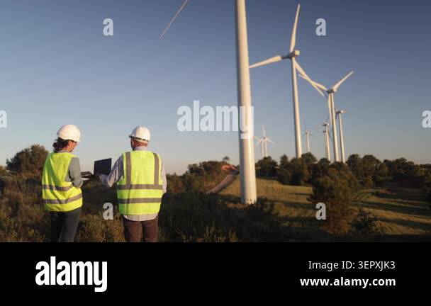 Two engineers wearing hard hats and safety vests are standing in a ...