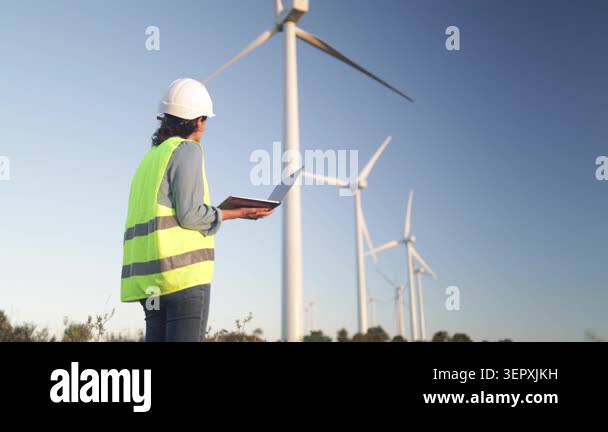 A woman wearing a hard hat and safety vest stands in a field of wind ...