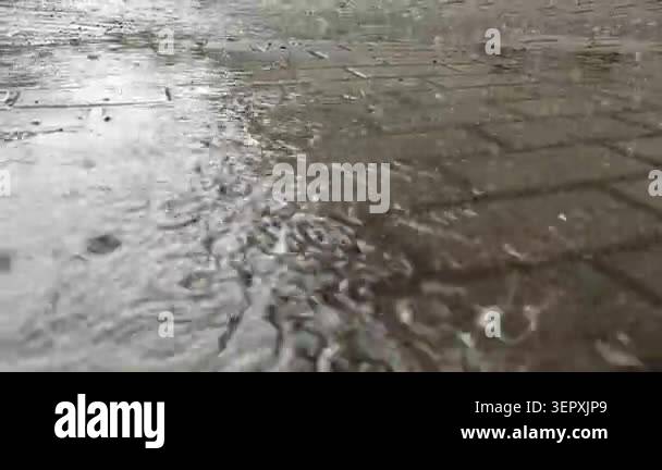 raindrops falling on paving stones during heavy rain with water puddles ...