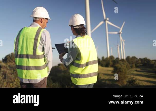 Two engineers wearing hard hats and high-visibility vests are looking ...