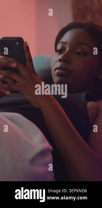 Young African American woman uses mobile phone while relaxing on couch ...