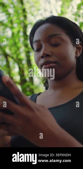 Young African American Woman reading mobile phone message in green park ...