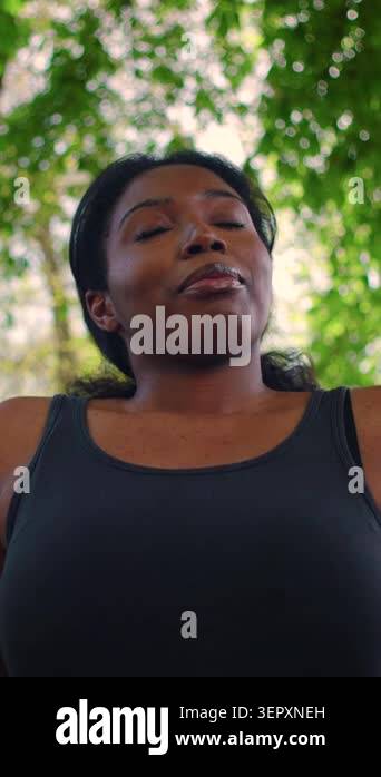 Young African American woman stands quietly in a park with soft smile ...
