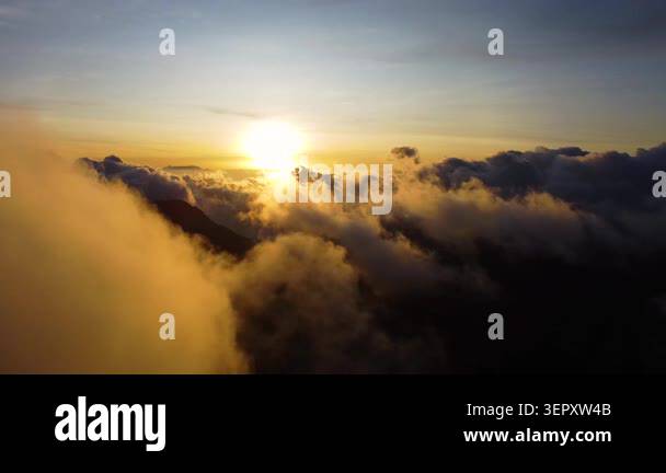Aerial footage flying above the clouds during a golden sunrise over the ...