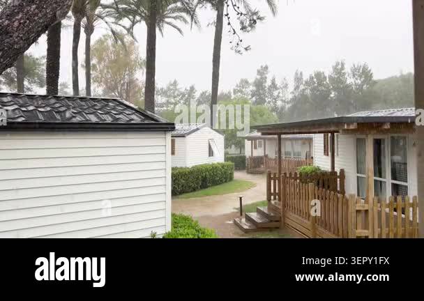 Heavy torrential rain falling on bungalows at a campsite with palm ...
