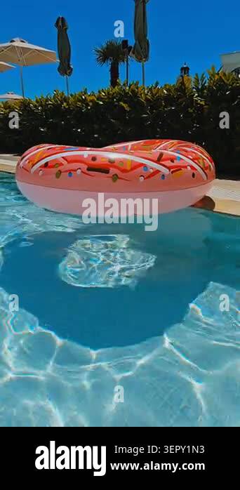 Pink donut inflatable pool float drifting in clear blue swimming pool ...
