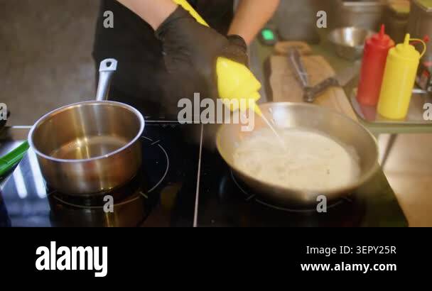 Kitchen work. Cooking pasta. Chef adding cream liquid bottle sauce on ...