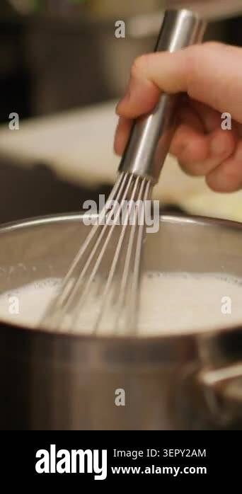 Vertical video. Culinary work. Whisking milk. Chef whipping boiling ...