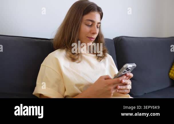 A smiling woman relaxes on a sofa with her phone in her hands in a ...