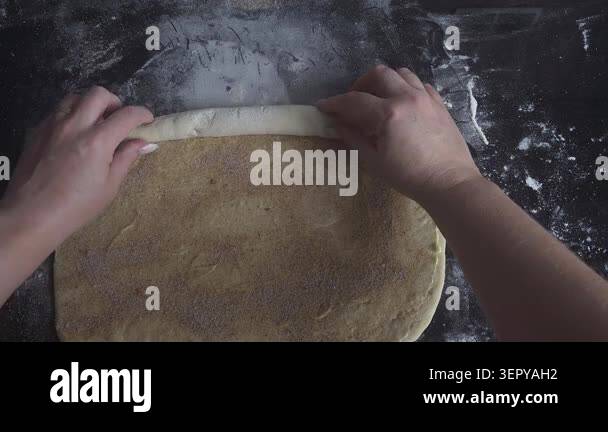 Top view of female hands rolling buttered dough covered with cinnamon ...