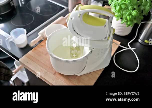 An electric stand mixer whisks fluffy egg white batter in a bowl in a ...