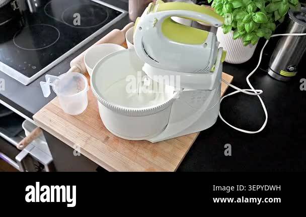 An electric stand mixer whips smooth white cake batter in a bowl on a ...
