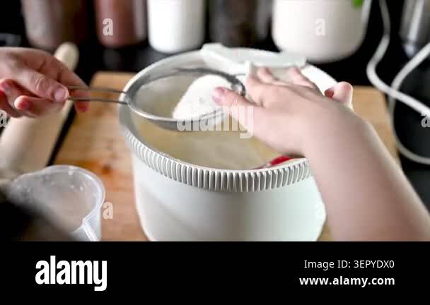 Close-up of hands sifting flour through a sieve into a bowl of batter ...