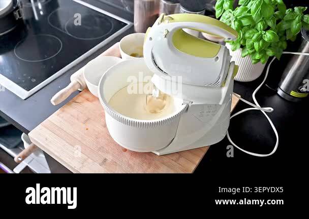 An electric stand mixer blends smooth pale yellow cake batter in a bowl ...