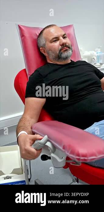 Vertical video of a mature man reclining in a red donation chair at a ...