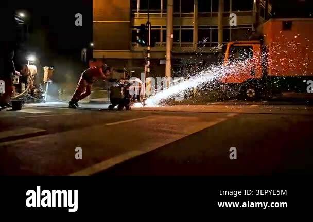 Wide night view of a worker pushing a rail grinding machine that throws ...