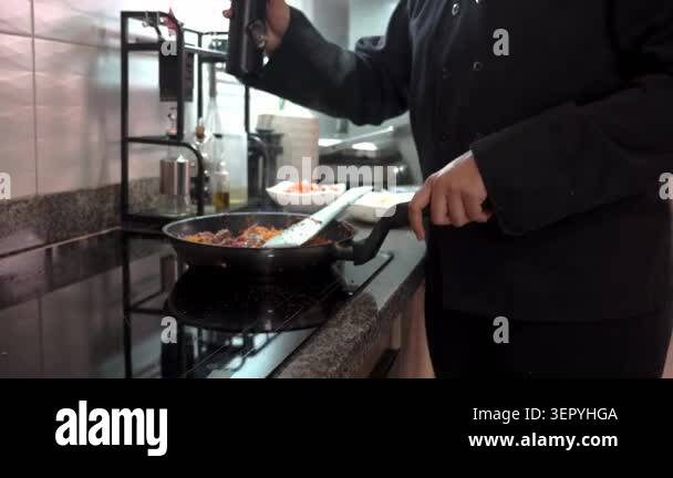 Female chef preparing a meal, stir-frying minced meat and seasoning it ...