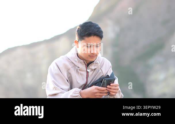 Young man looking at his smartphone while standing outdoors in a ...