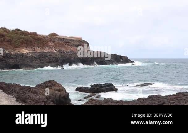 A beautiful atmospheric view of a volcanic cliff with waves crashing ...