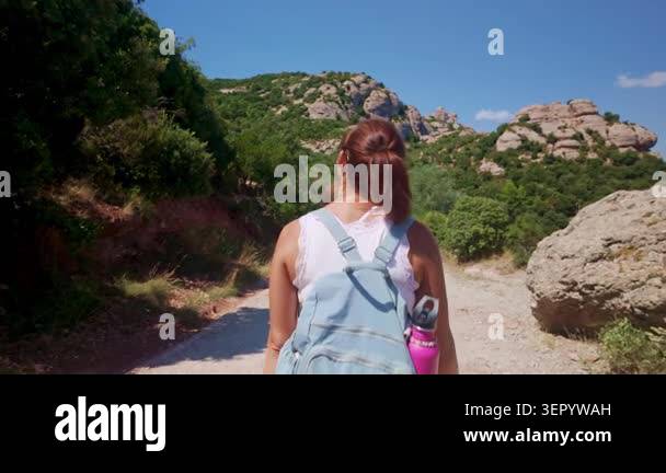 Young woman with a backpack walking on a dirt path during a hike in the ...