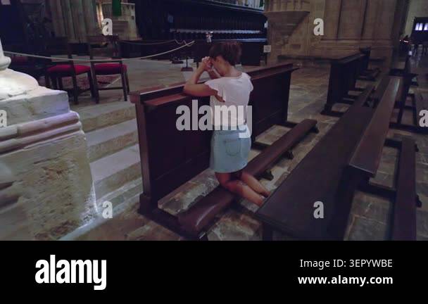 Pensive woman kneeling on a wooden pew inside a catholic church with ...