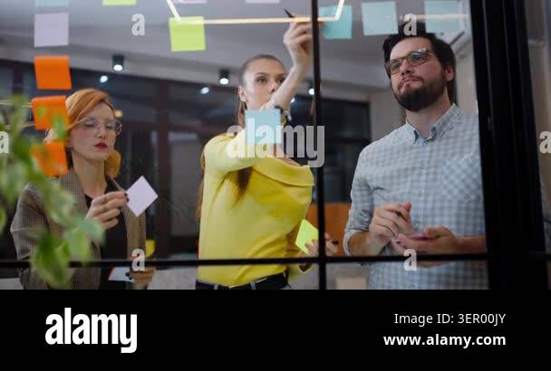 Group collaborates using sticky notes on glass board at office. They ...