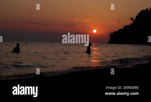 Silhouetted figures walking in warm sunset light, reflected on gentle ...