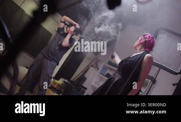 A model with pink hair poses in a studio while a photographer takes ...