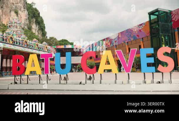 People walk around Batu Caves in Malaysia looking at colorful signs ...