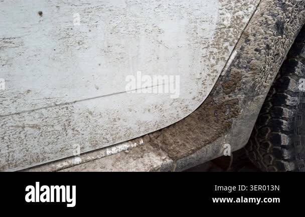 A white car drives through muddy trails, splashing dirt onto its side ...