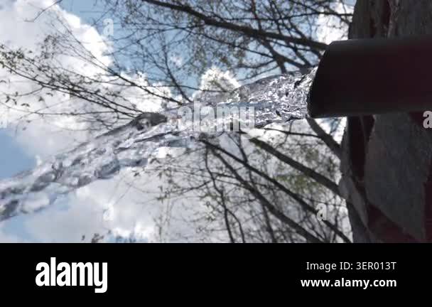 Water flows from a pipe in a park. The sky is mostly cloudy with some ...