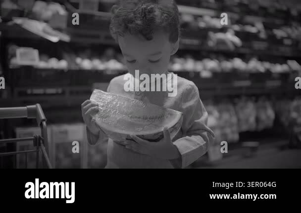 Young child standing beside a shopping cart in a supermarket produce ...