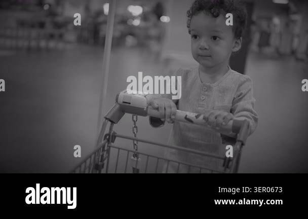 Candid black-and-white shot of a young child pushing a small metal ...