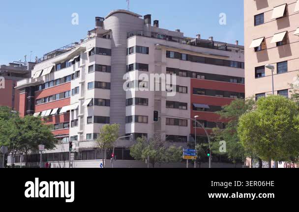 Urban building with red and white facade. Green trees line the street ...