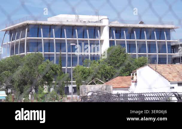 Modern glass building under construction behind chain-link fence. Trees ...