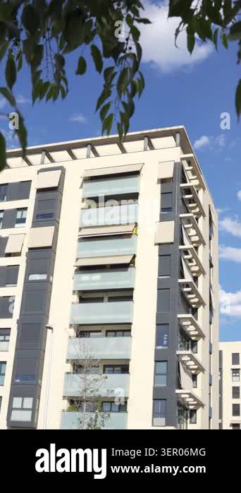 Modern apartment building rises under clear blue sky. Green tree ...