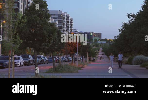 Pedestrians walk along a tree-lined urban boulevard during blue hour ...
