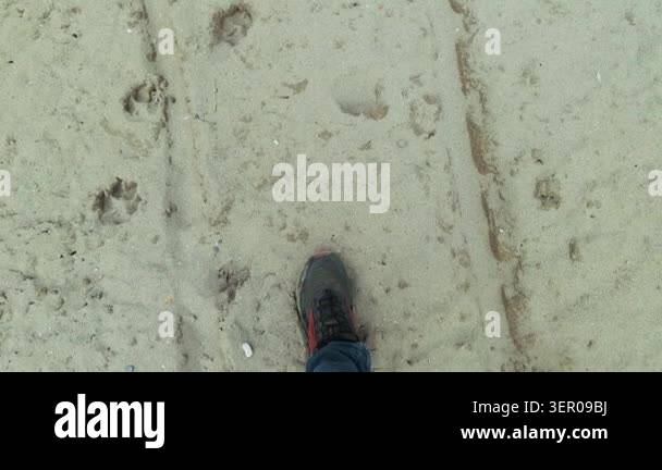A man walking alone on the sandy beach, leaving footprints behind while ...